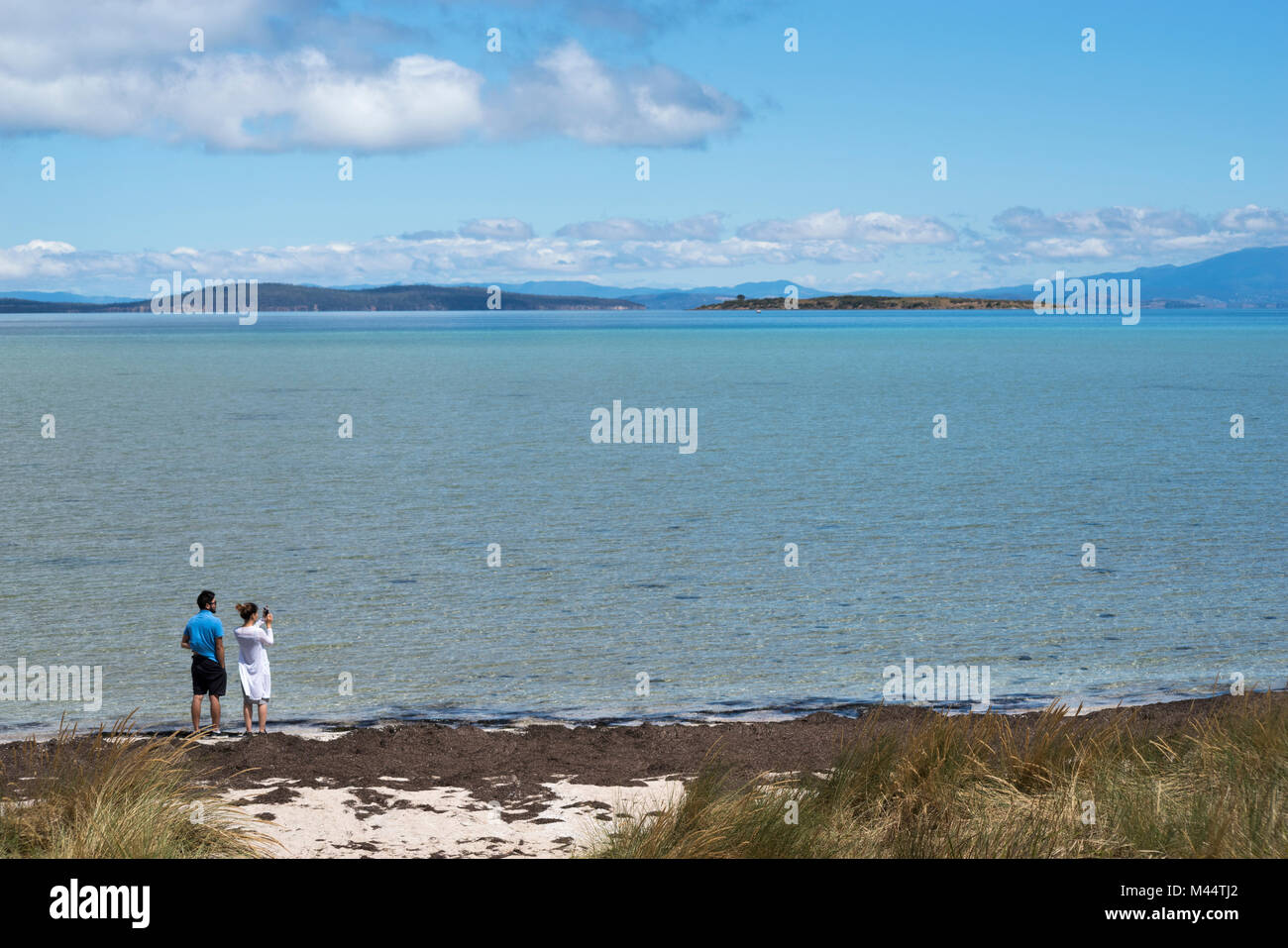 A young couple taking a photo of the view at Carlyle Beach, Dunalley ...
