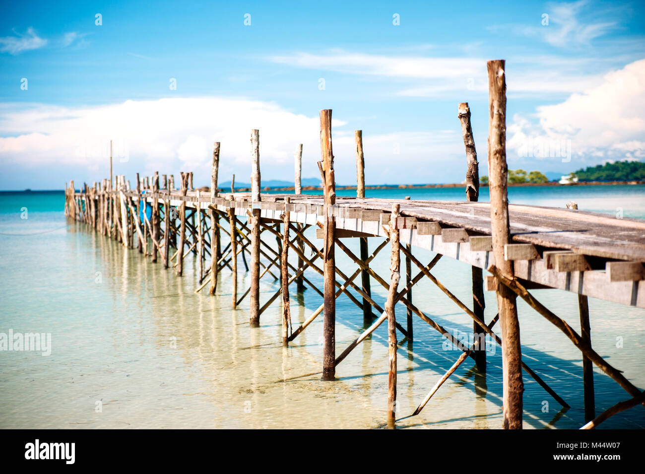 wooden long pier into the sea. blue clear water and sky with clouds ...