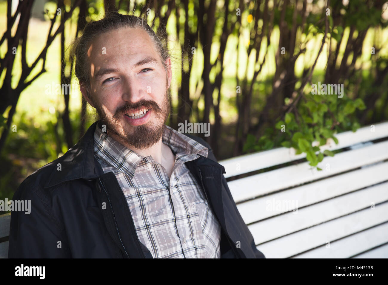 Young bearded smiling man on white bench in summer park, outdoor ...