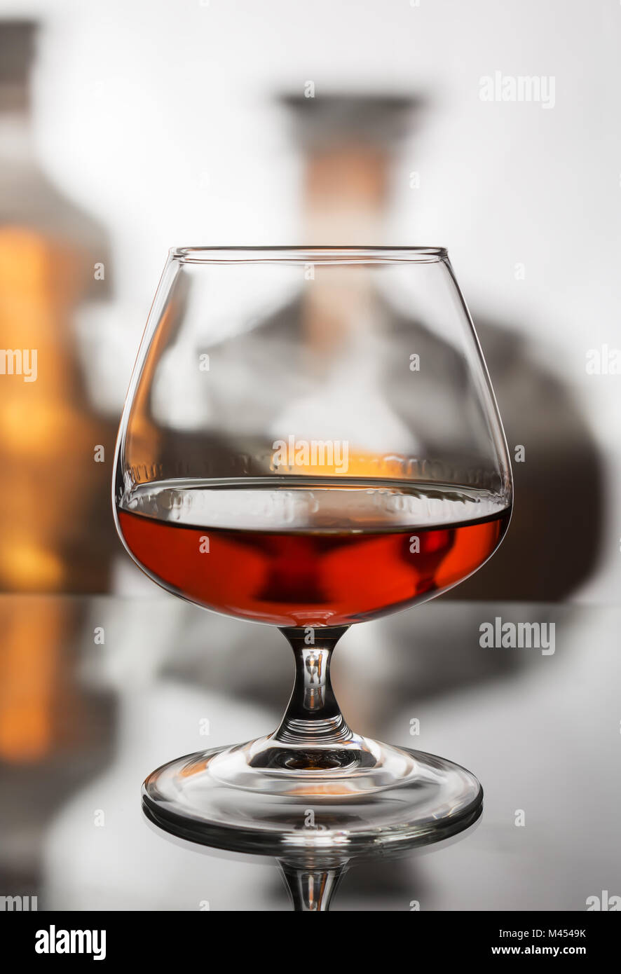 A glass of strong aromatic brandy on the background of two bottles ...