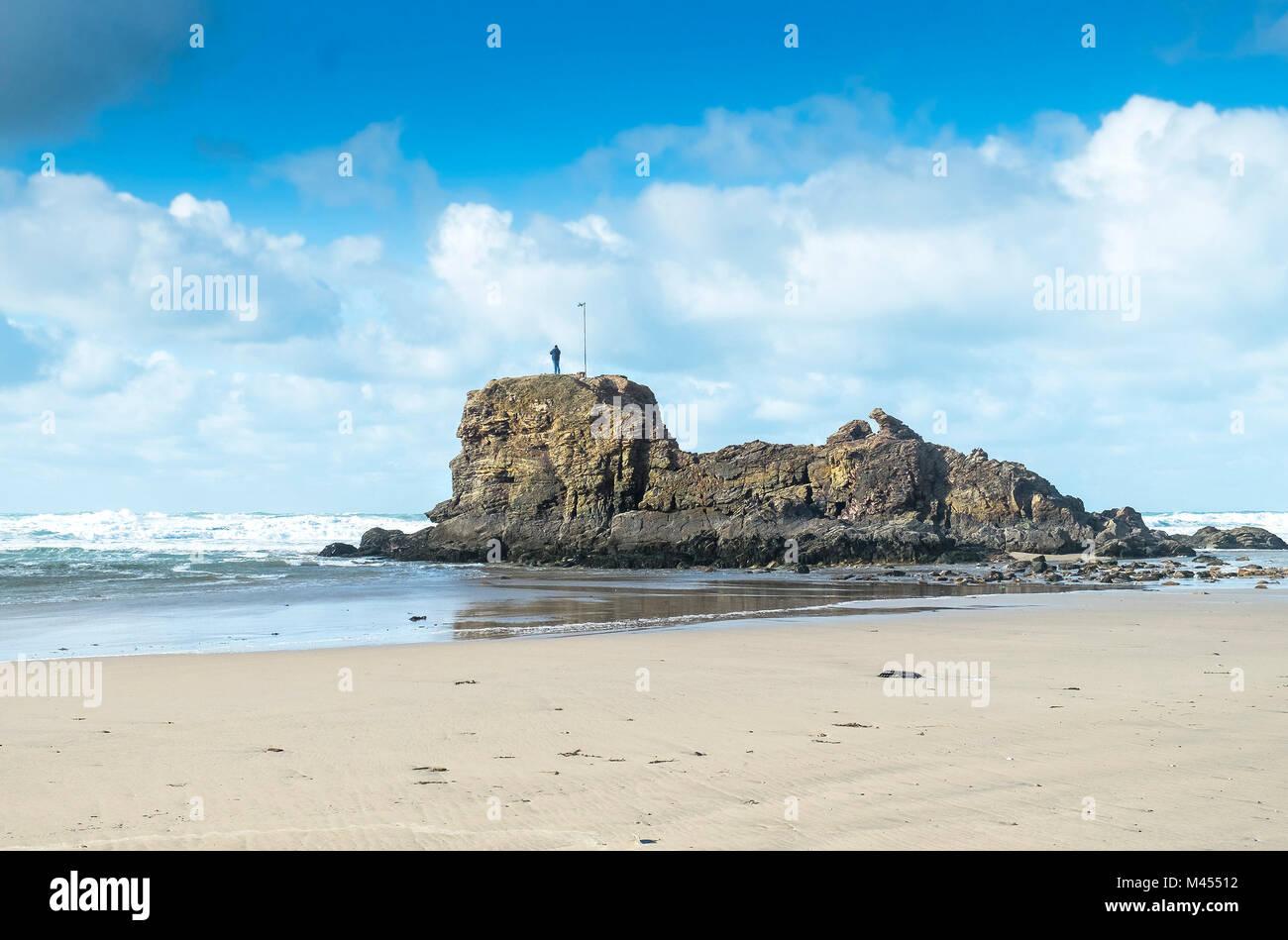 A figure standing on top of Chapel Rock on Perranporth Beach in ...
