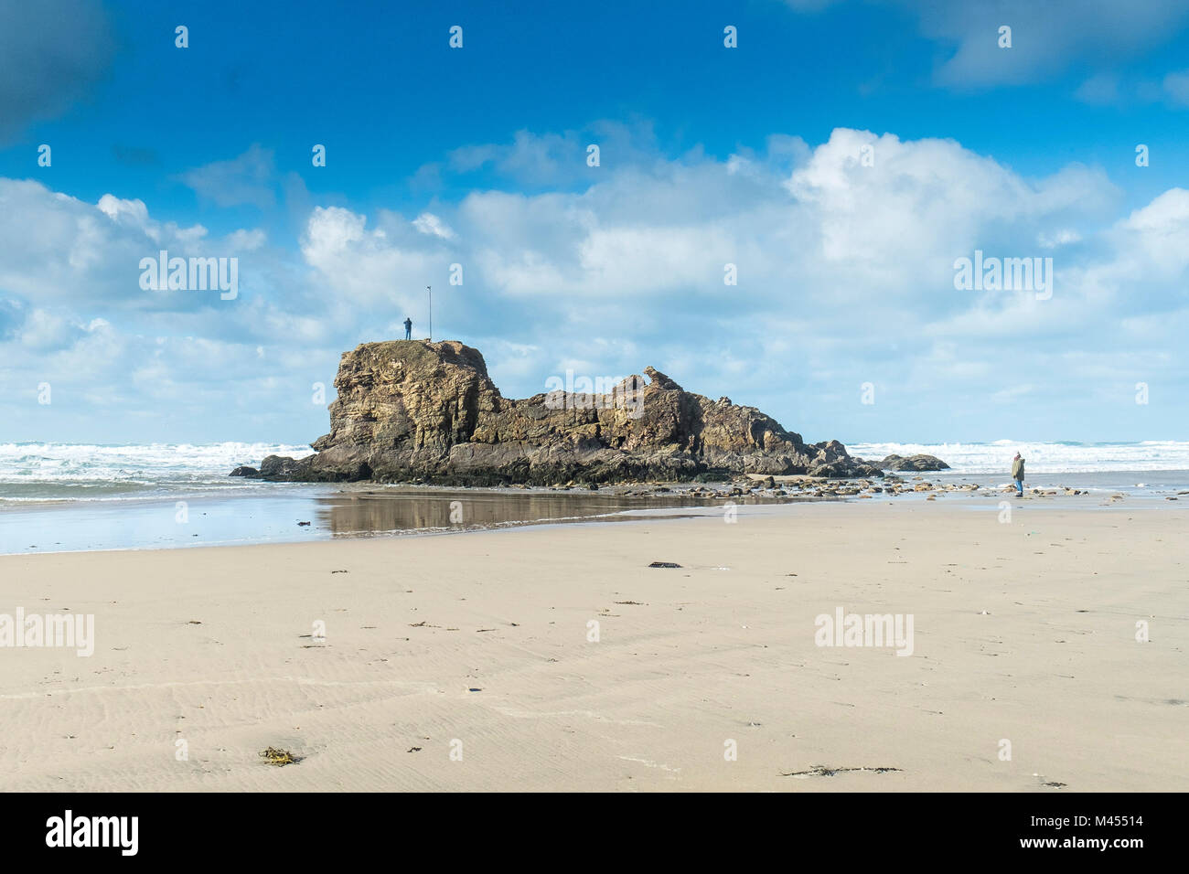 A figure standing on top of Chapel Rock on Perranporth Beach Cornwall ...