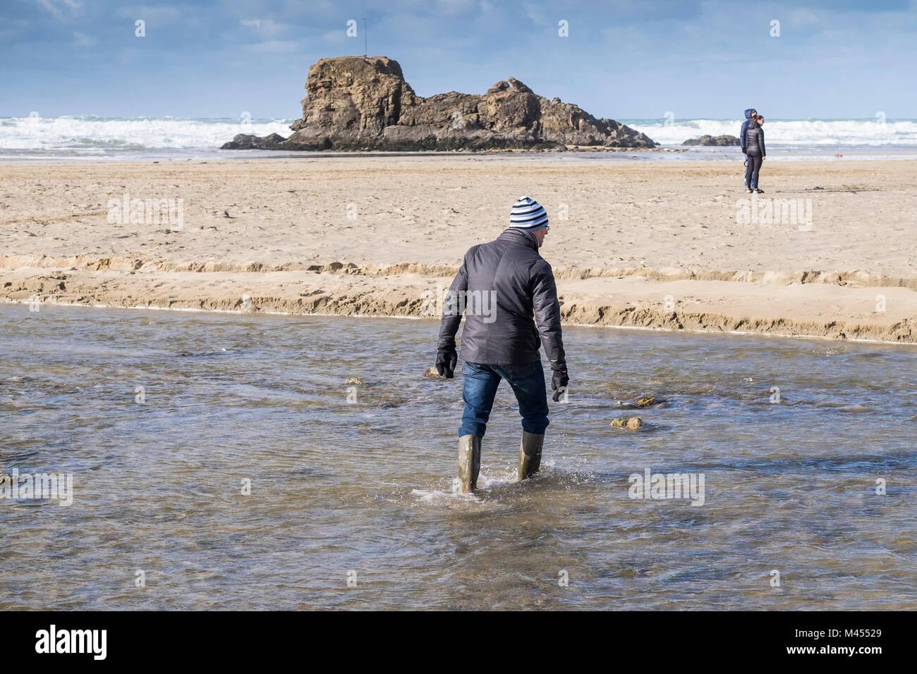 A man wading across a river on Perranporth Beach in Cornwall UK Stock ...