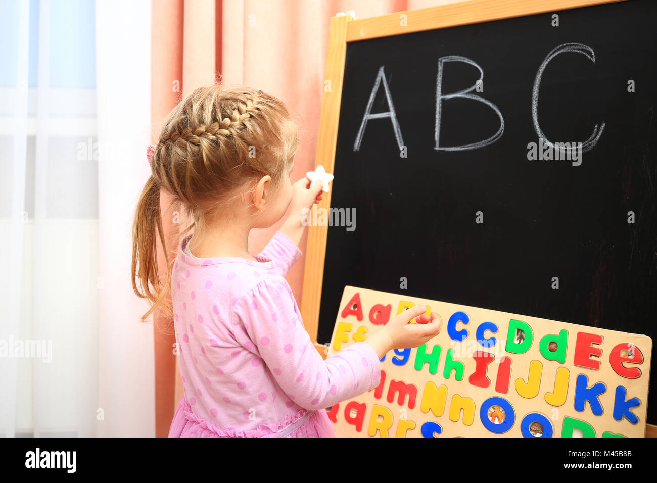 Little girl learns write letters on blackboard. Preschooler study ABC ...
