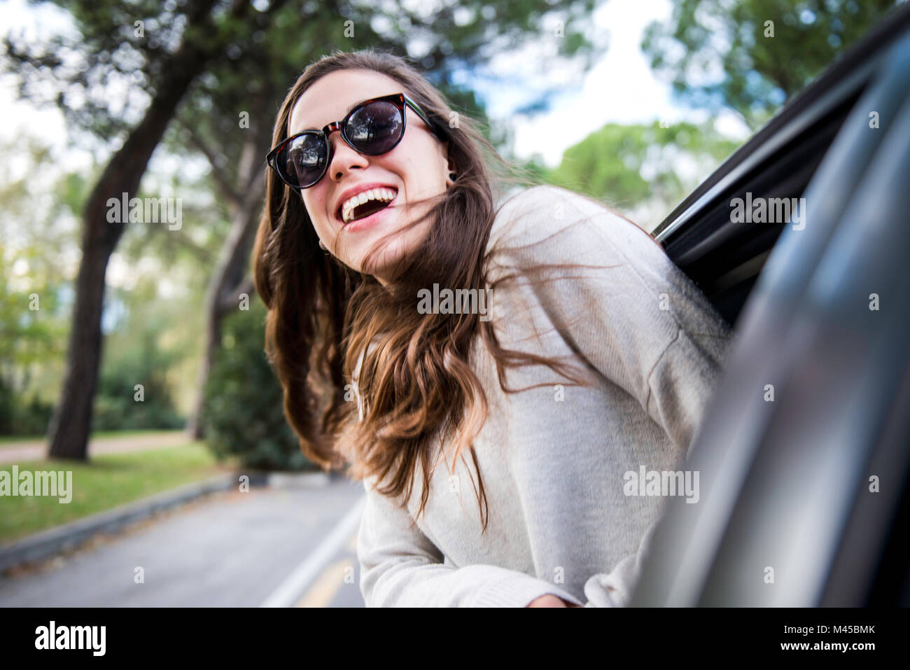 Happy young woman on road trip leaning out of car window Stock Photo ...