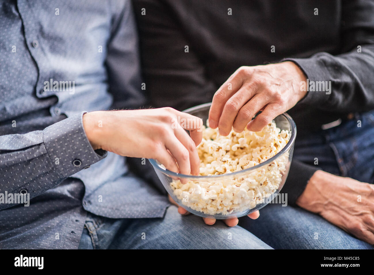 Son and his senior father eating popcorn at home Stock Photo - Alamy