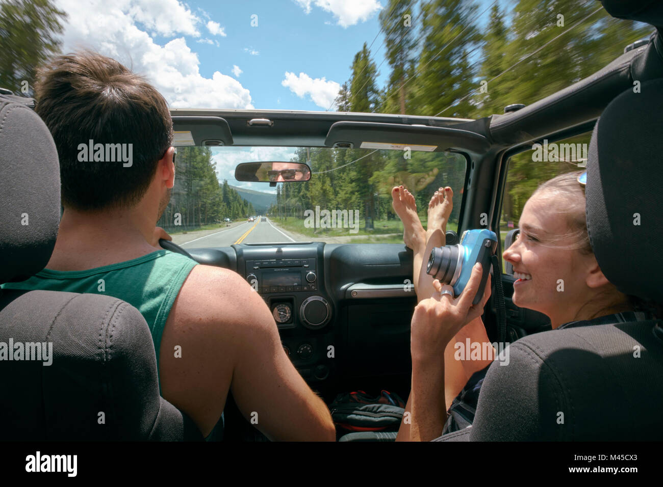 Young woman with instant camera driving on road trip with boyfriend ...