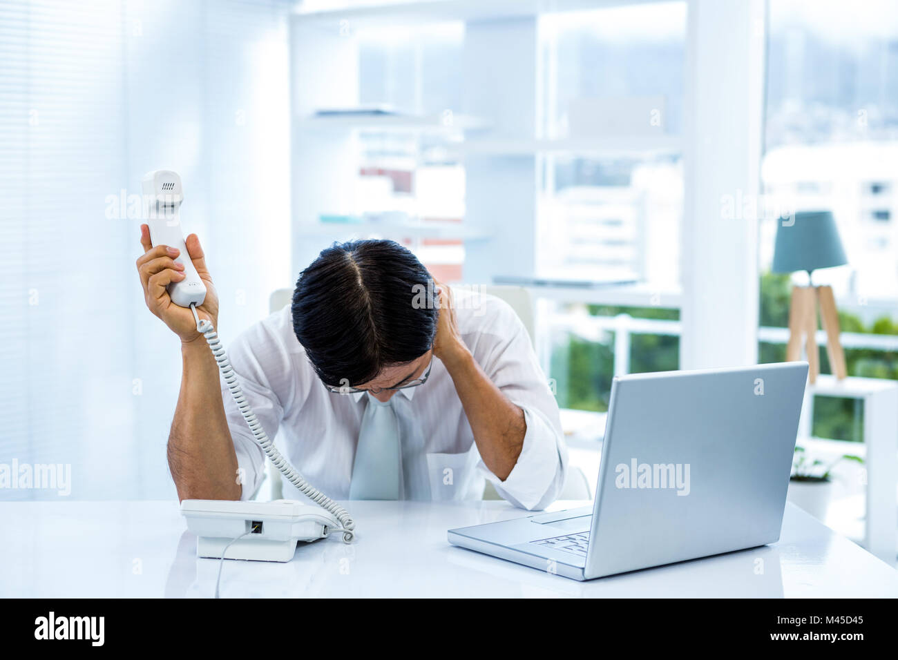 Overwhelmed asian businessman answering the phone Stock Photo - Alamy