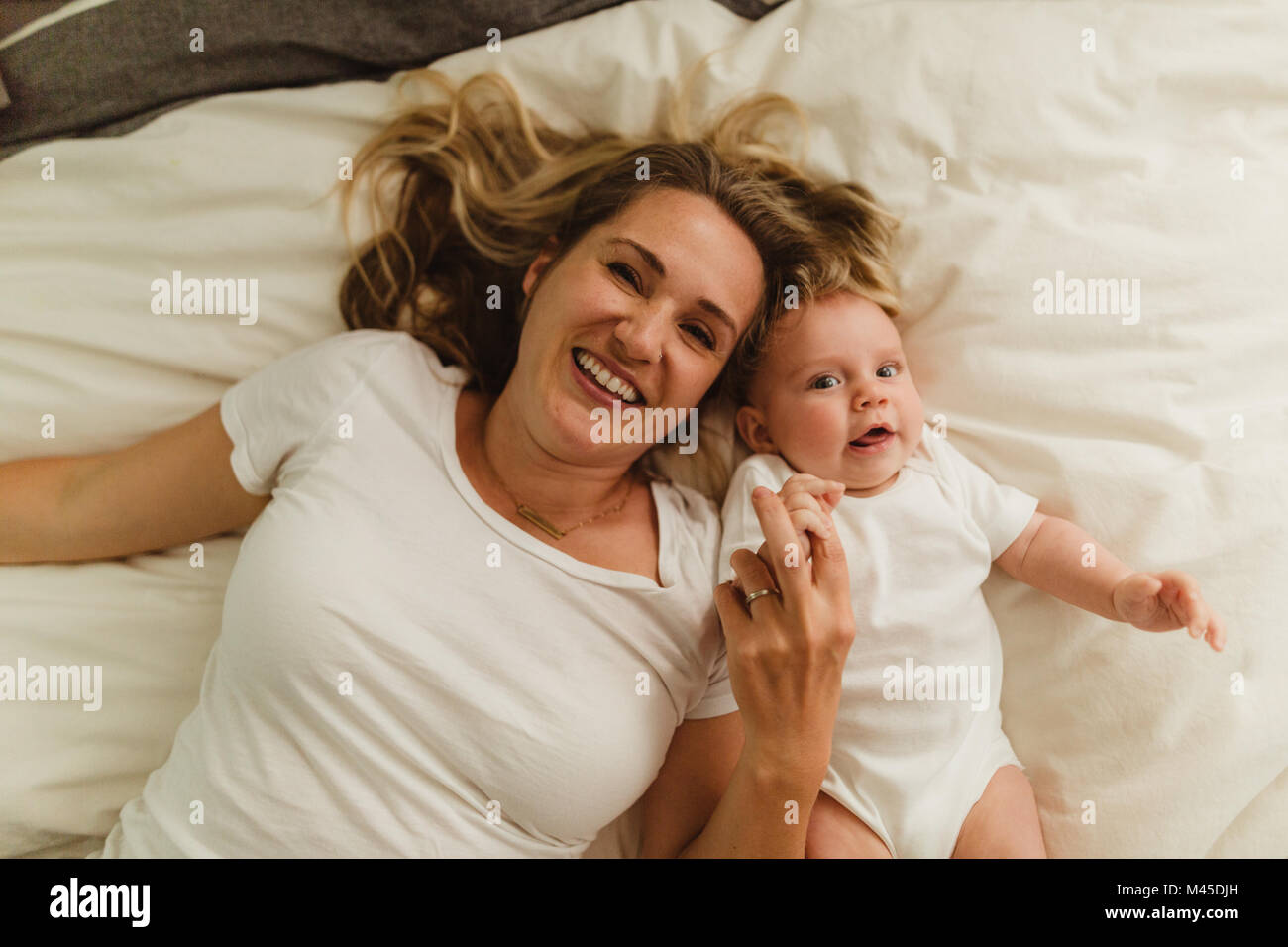 Overhead portrait of woman and baby daughter lying on bed holding hands Stock Photo - Alamy