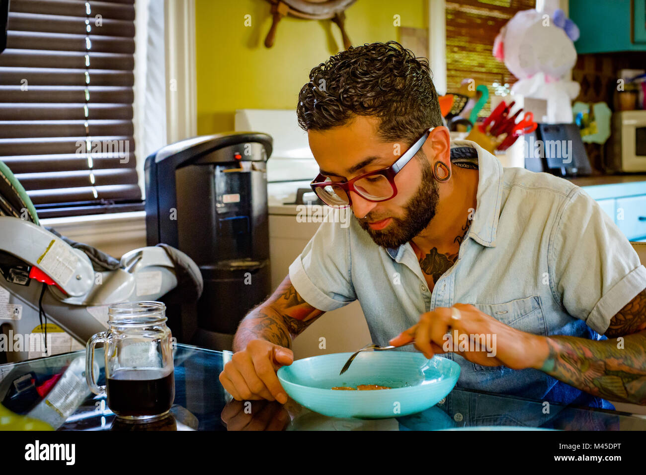 Young man in spectacles eating at kitchen table Stock Photo - Alamy