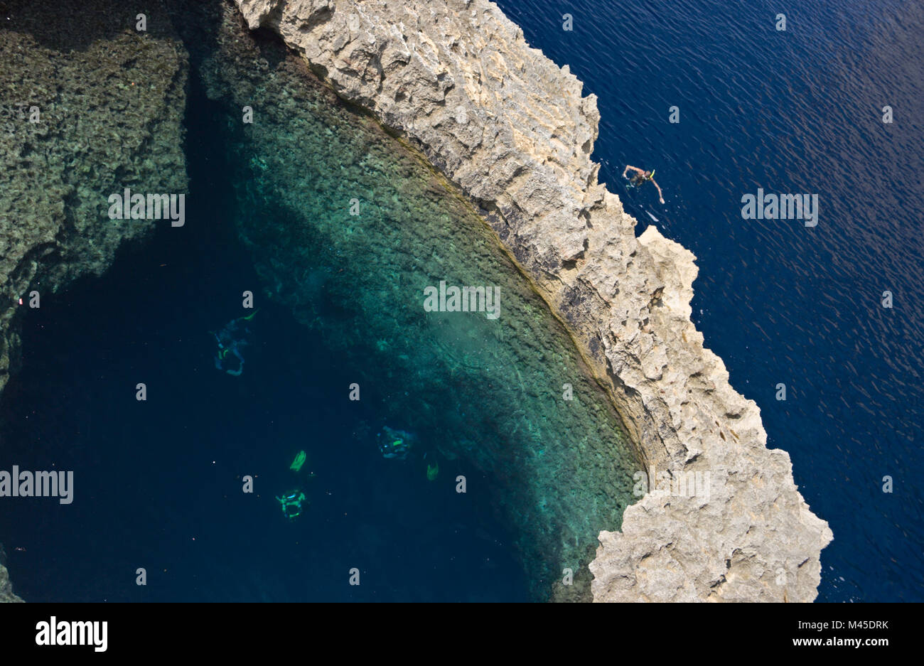 Some divers and a snorkeler are examining an underwater stone arch ...