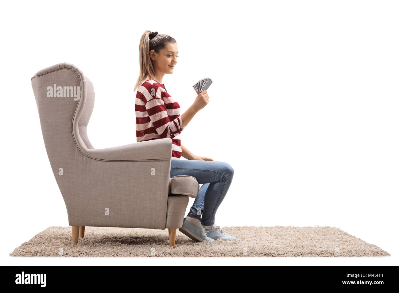 Young woman with playing cards sitting in an armchair isolated on white ...