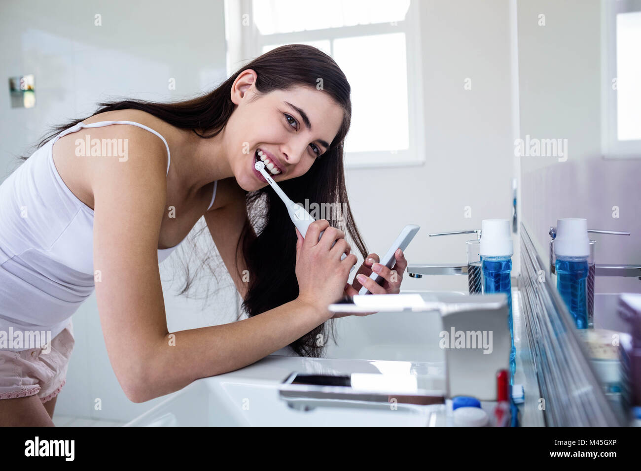 Brunette using smartphone while brushing teeth Stock Photo - Alamy