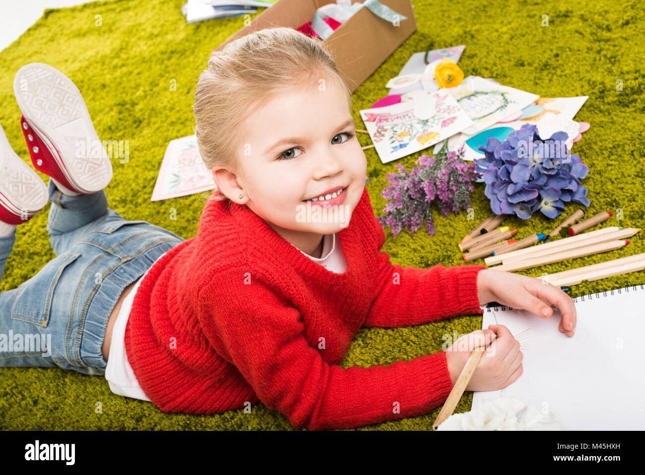 smiling little child drawing with color pencils on green soft carpet ...