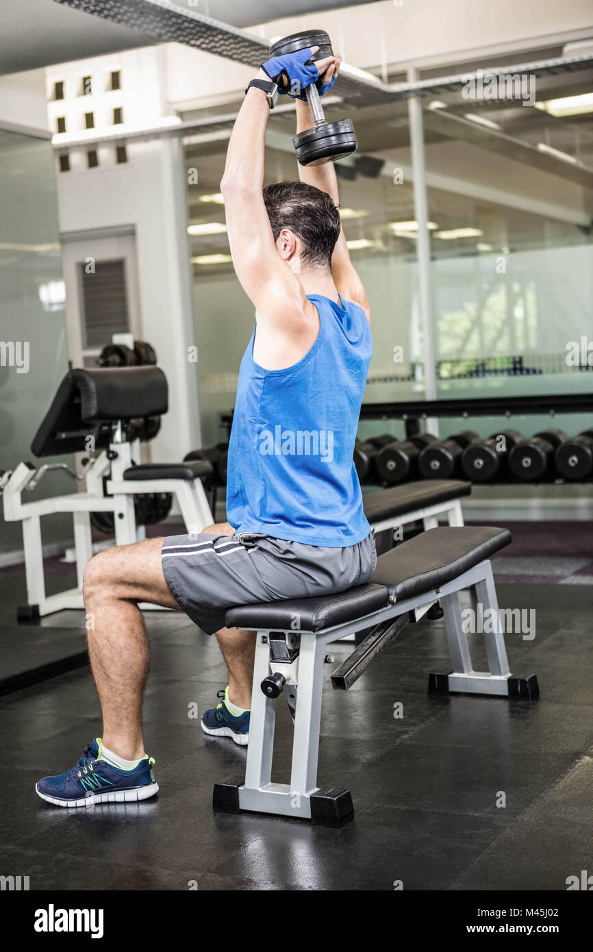 Muscular man lifting dumbbell while sitting on bench Stock Photo - Alamy