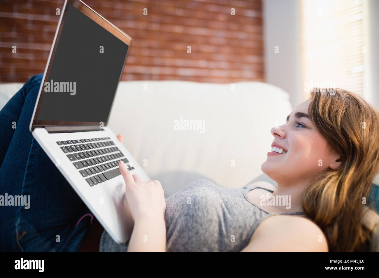 Pretty woman lying on the couch using her laptop Stock Photo - Alamy