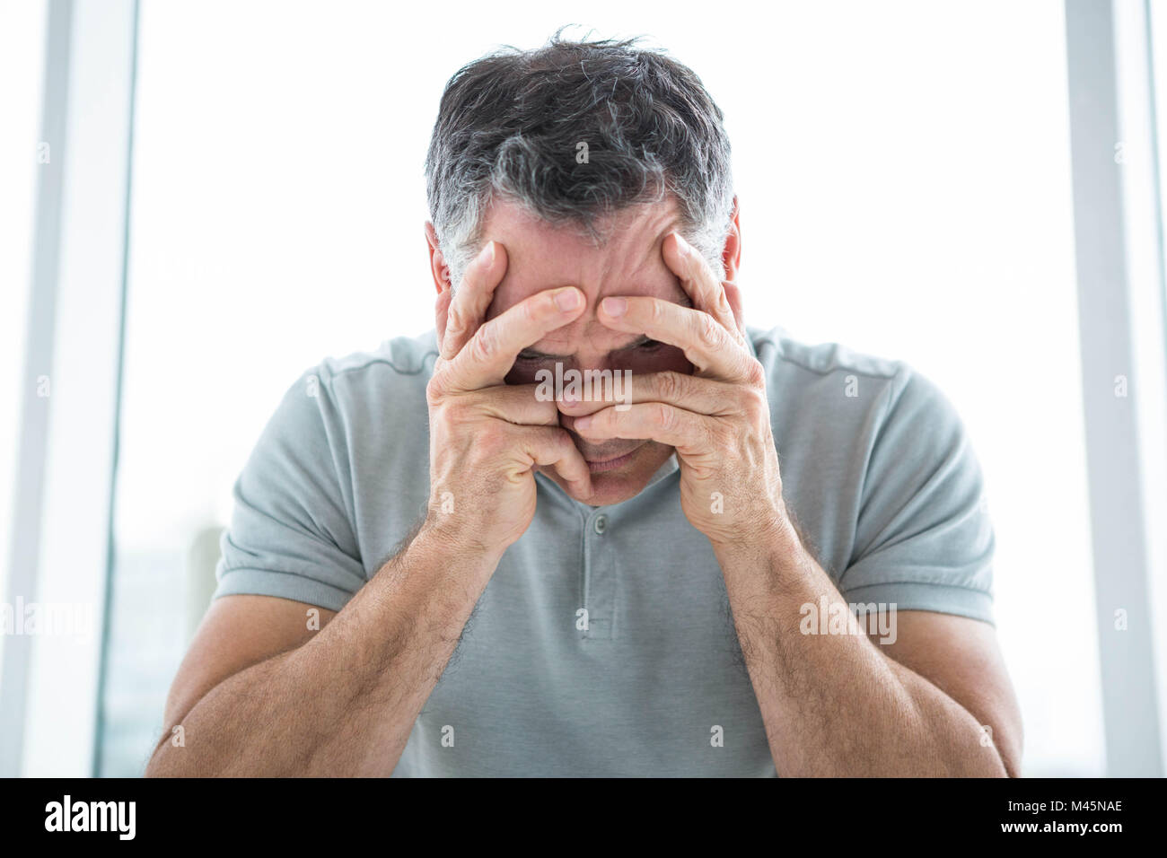 Tensed man sitting and thinking against window Stock Photo - Alamy