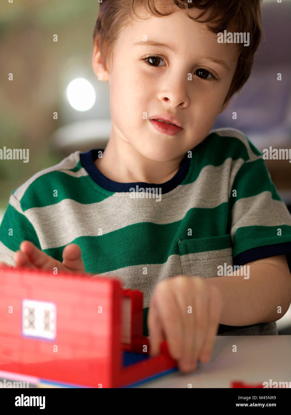 Caucasian five year old boy building a red house out of lego bricks ...