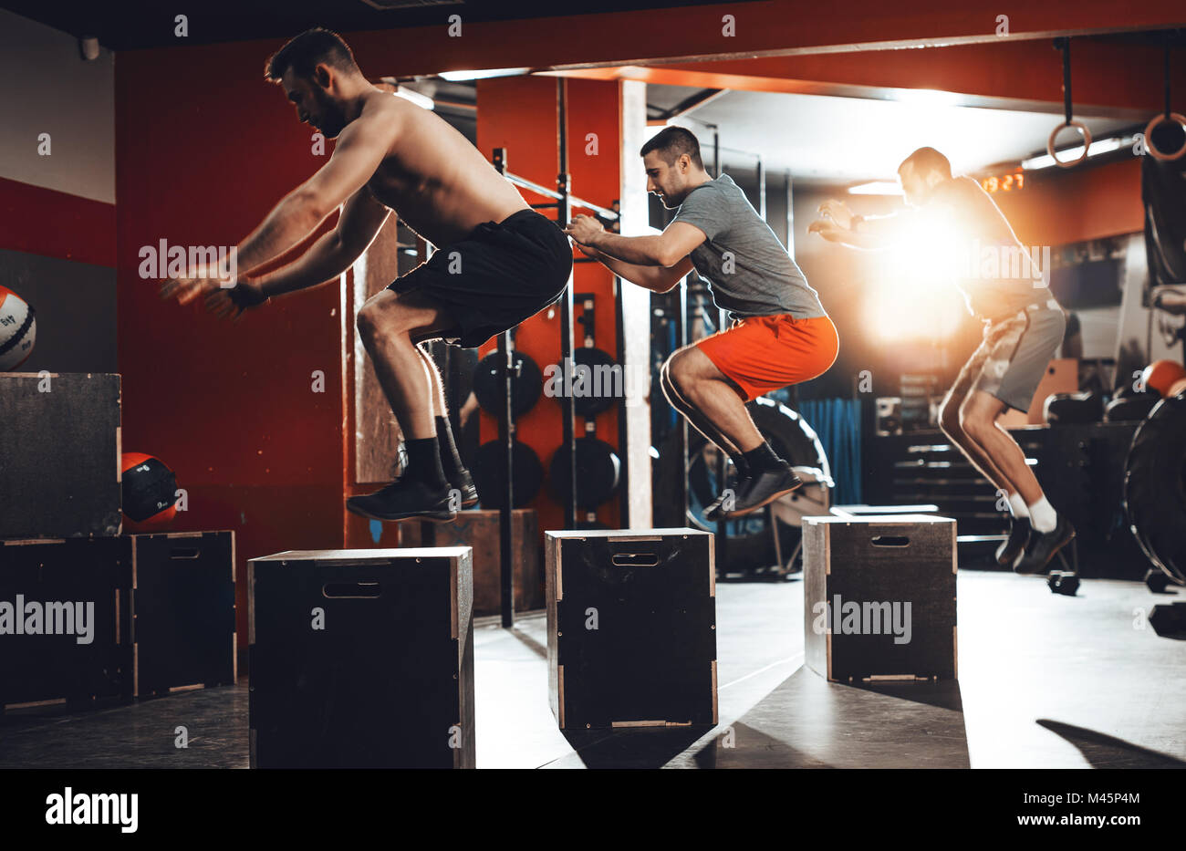 Three young male friends doing hard exercise at the gym. They are ...