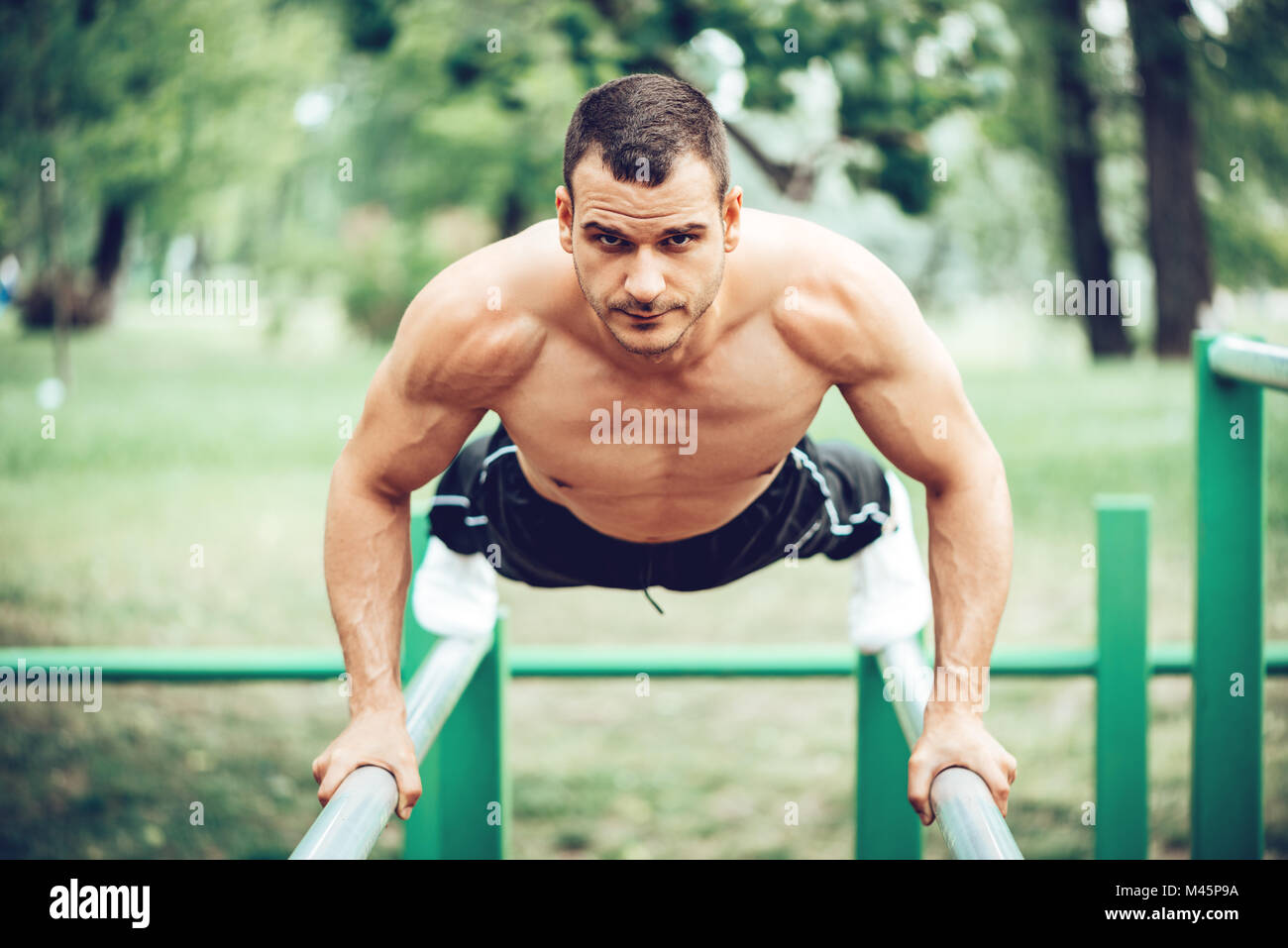 Young sportsman doing push-up exercise in the park. Looking at camera ...