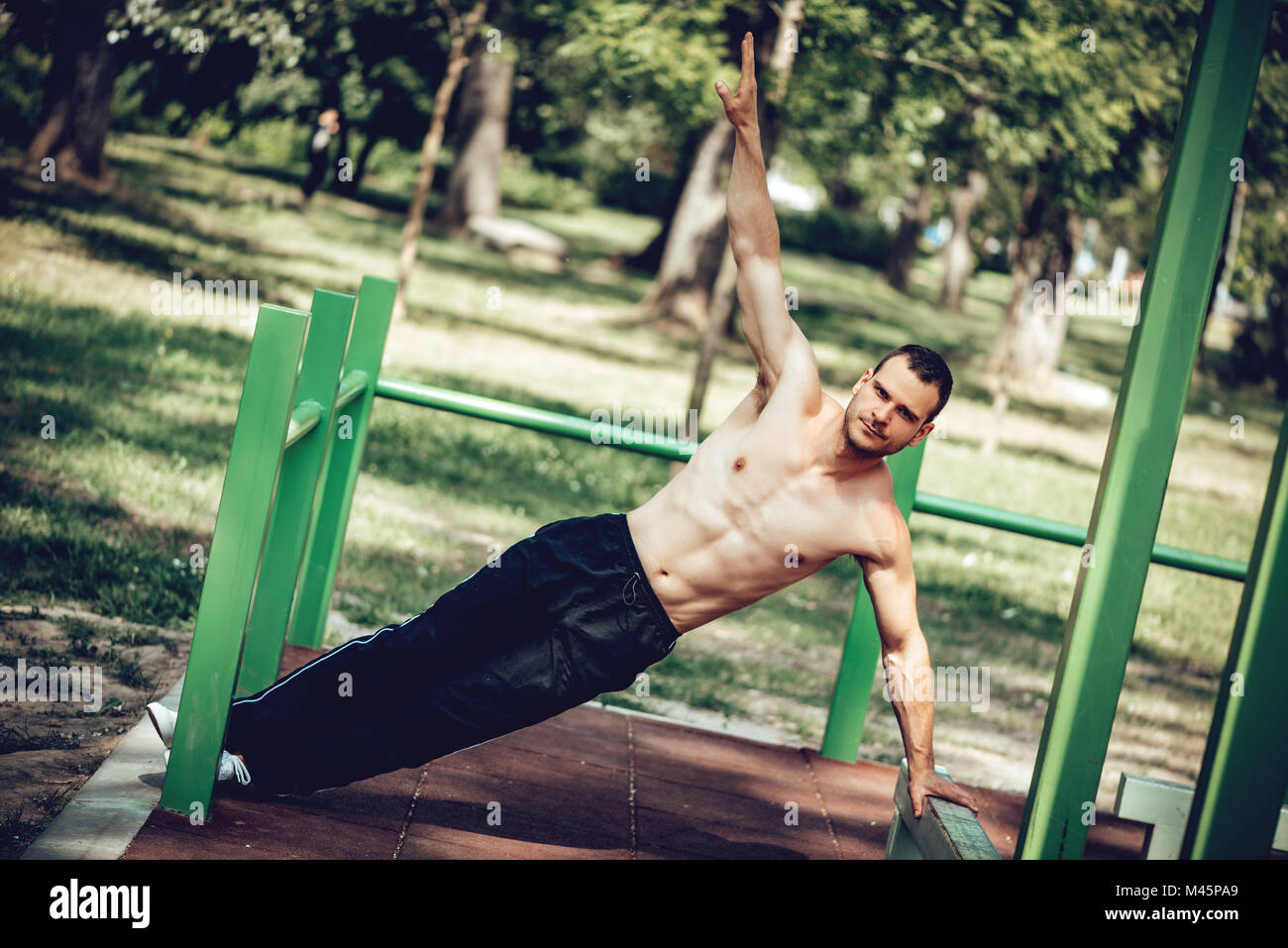 Young sportsman doing hard exercise in the park. One hand is holding ...