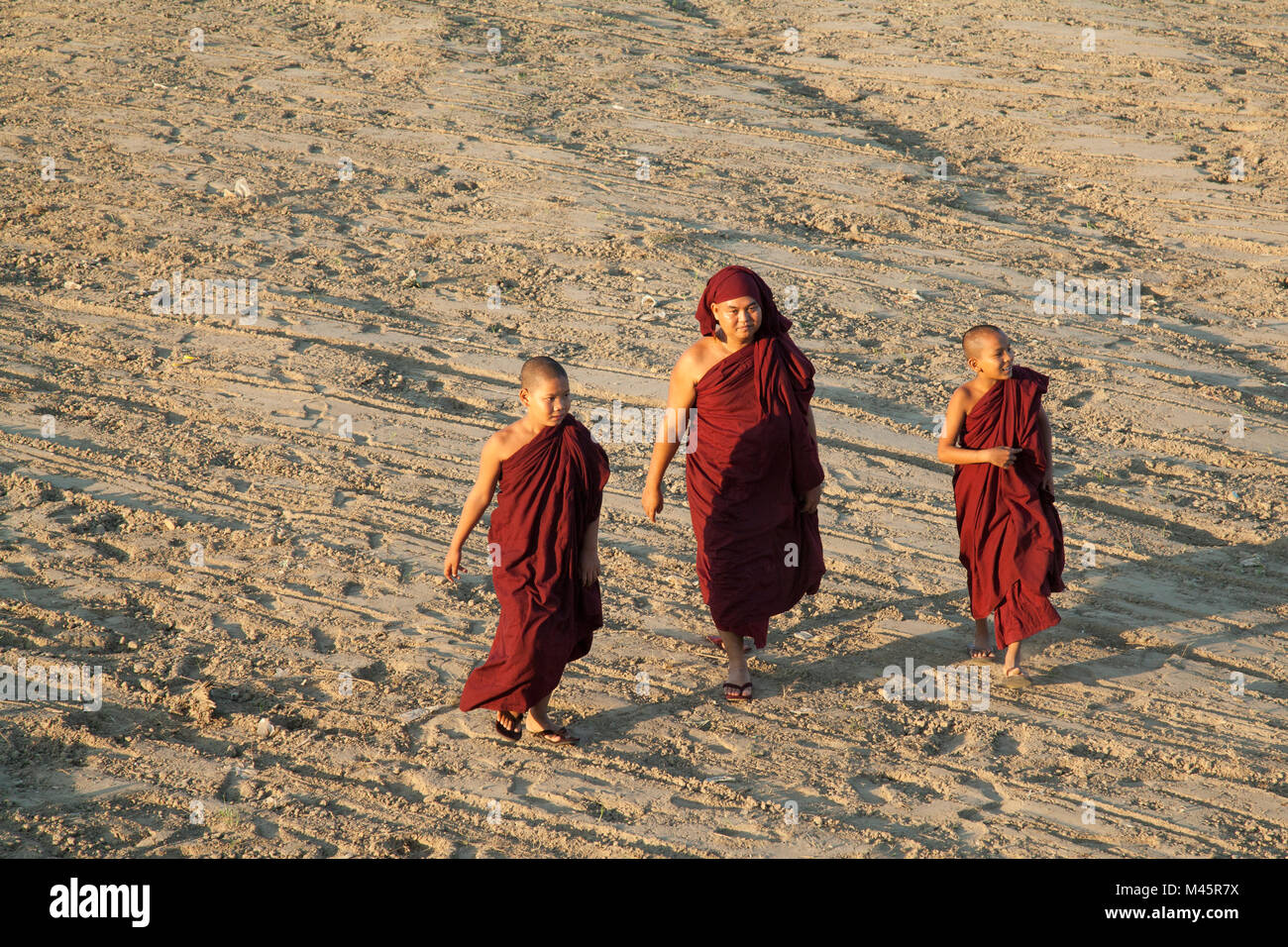 Young monks walking on the sandy shoreline near U Bein Bridge in ...