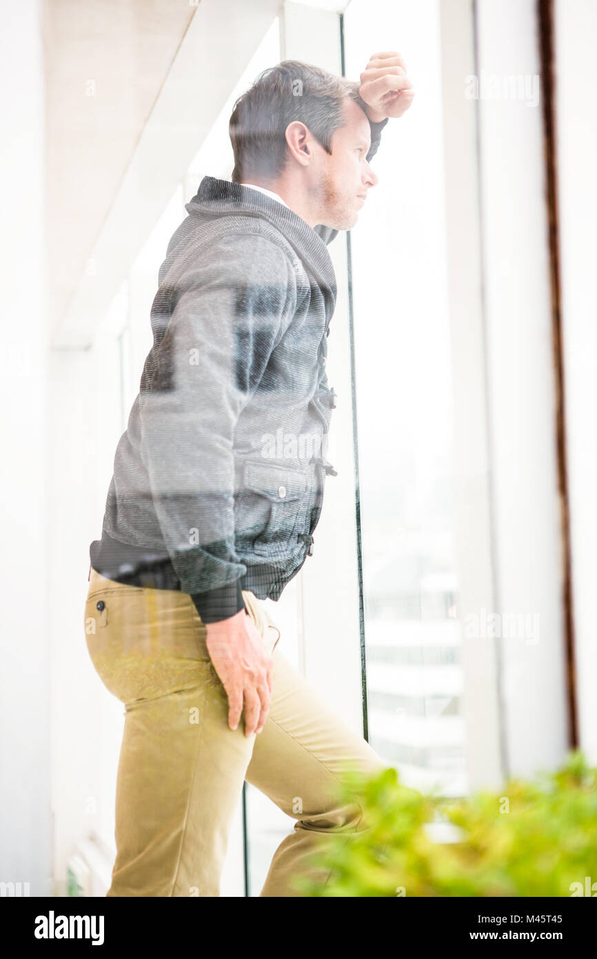 Thoughtful businessman leaning on glass window Stock Photo - Alamy