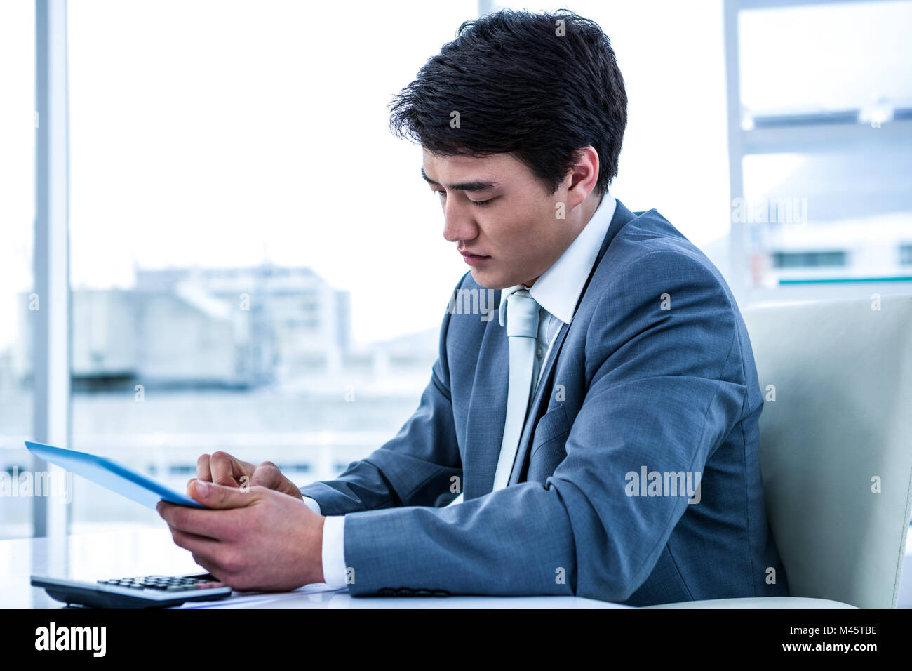 Concentrated asian businessman using his tablet Stock Photo - Alamy