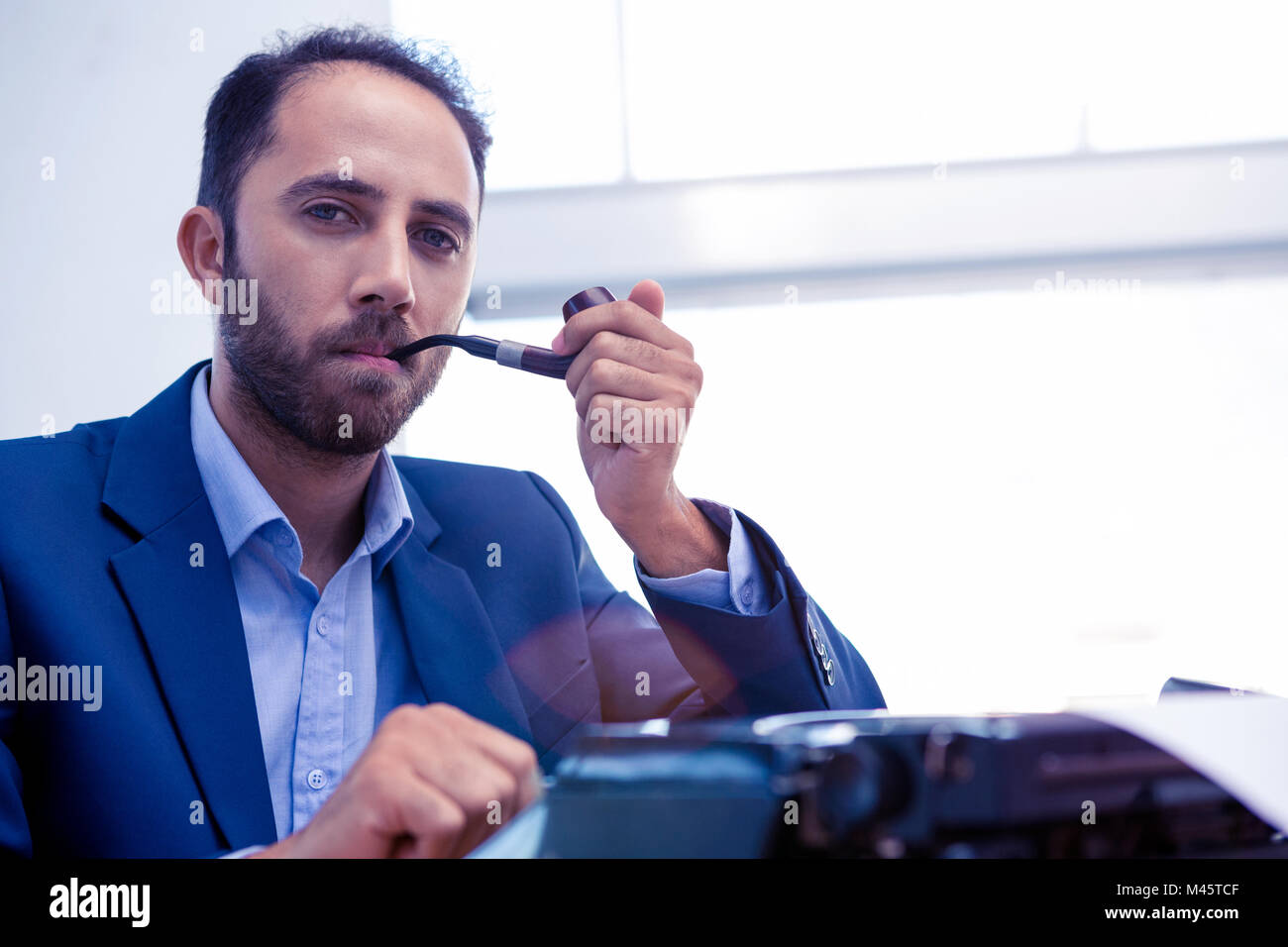 Portrait of businessman using typewriter while holding smoking pipe ...