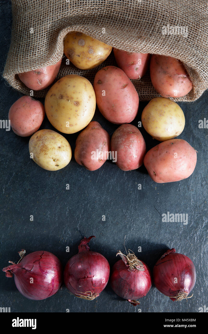 Red and Gold potatoes in hessian sack with red onions on slate table ...