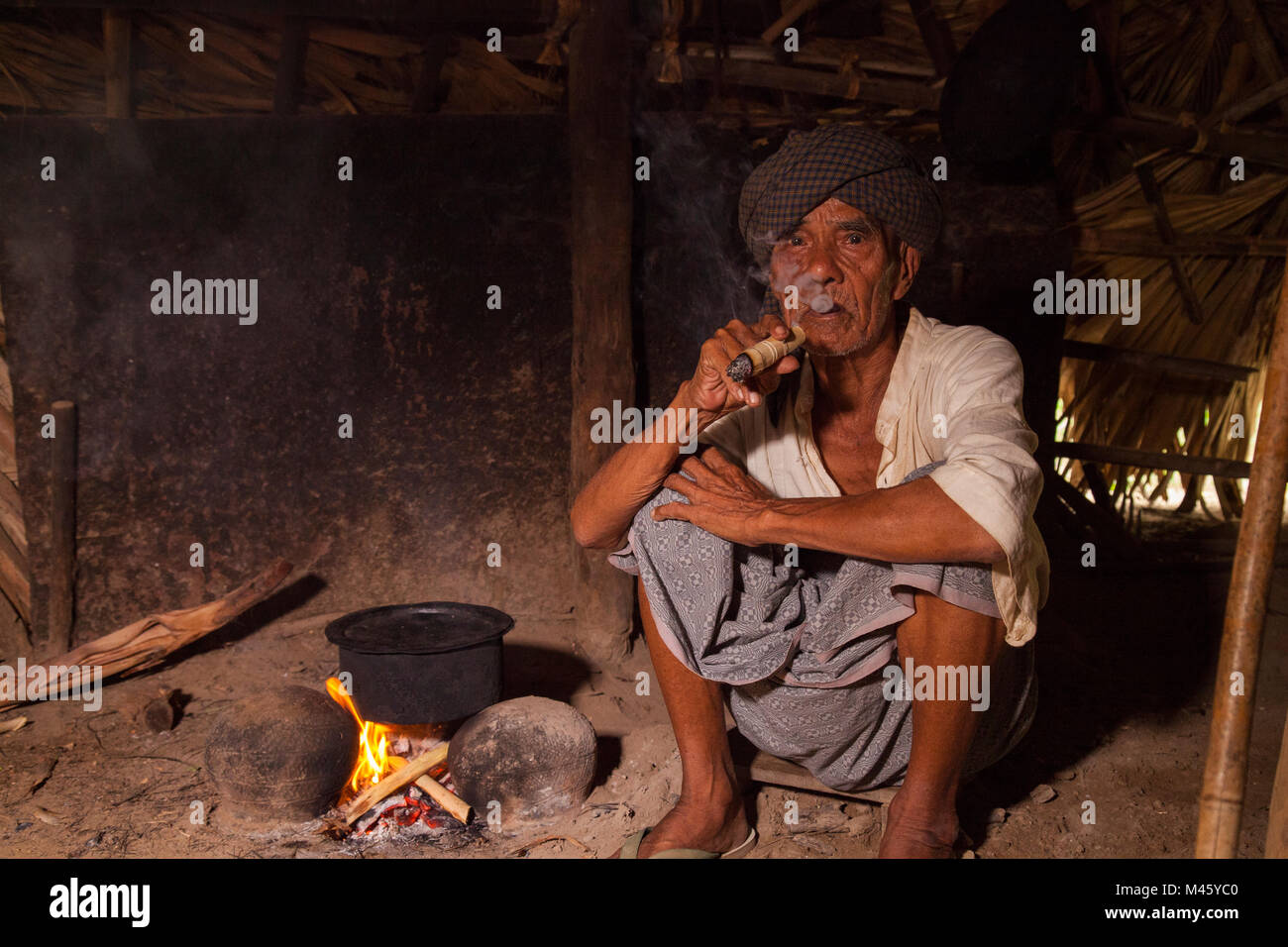 Local Burmese man smoking cigar by fire in his home in Bagan Myanmar ...