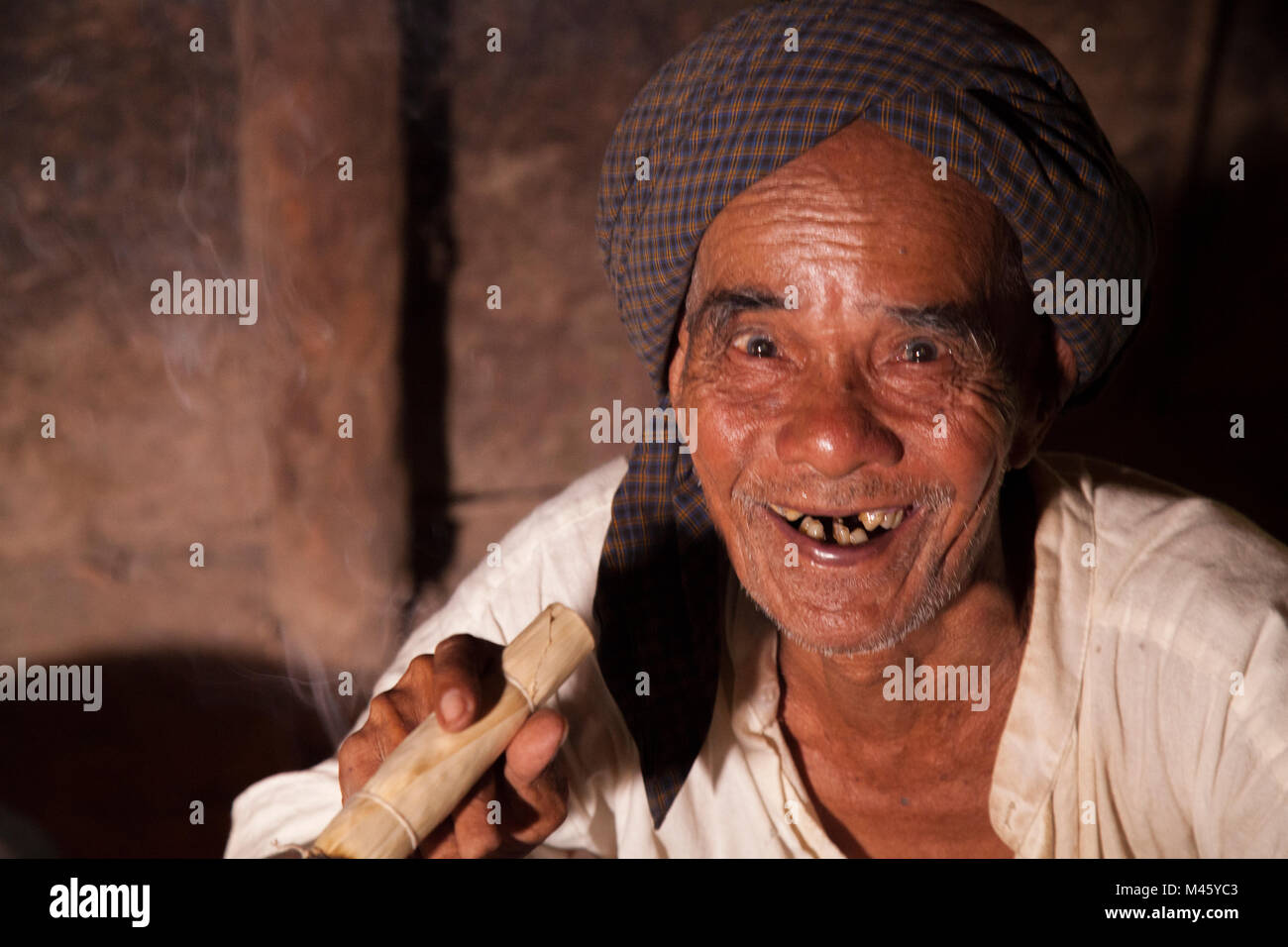 Local Burmese man smoking cigar by fire in his home in Bagan Myanmar ...