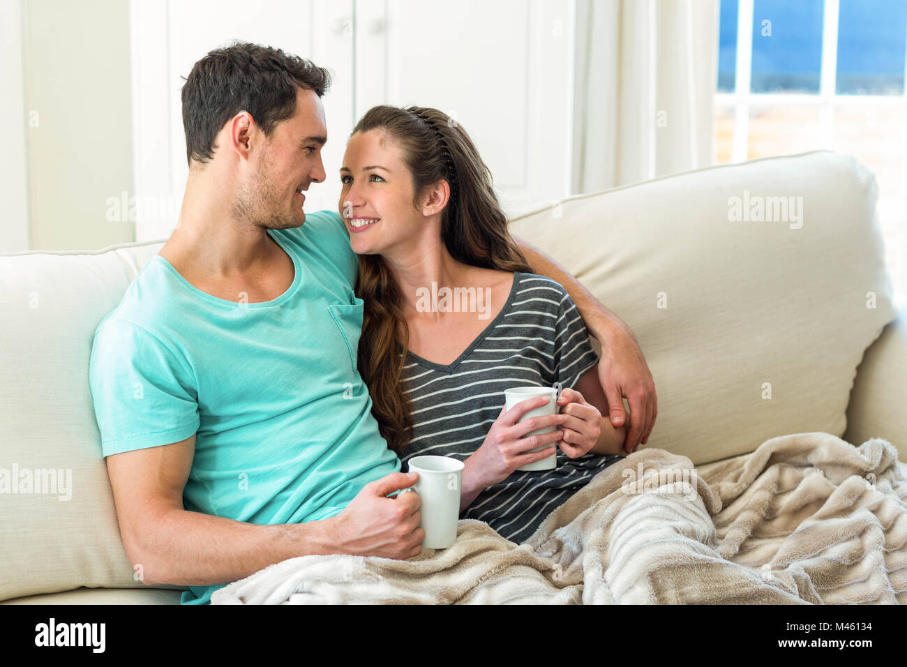 Young couple cuddling on sofa while having coffee Stock Photo - Alamy