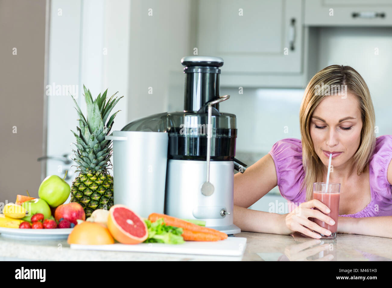 Blonde woman drinking a smoothie in the kitchen Stock Photo - Alamy