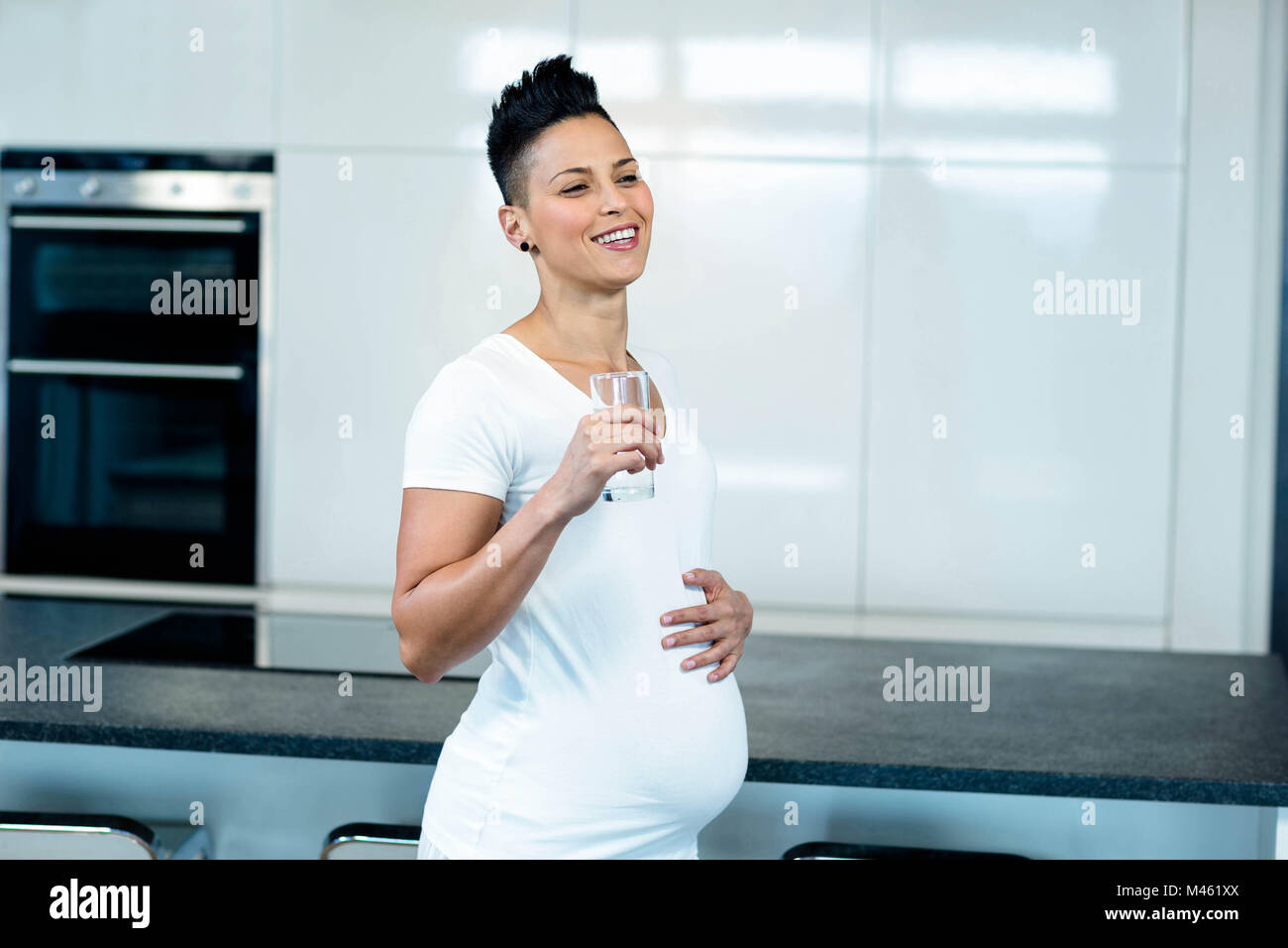 Smiling pregnant woman drinking water in kitchen Stock Photo - Alamy