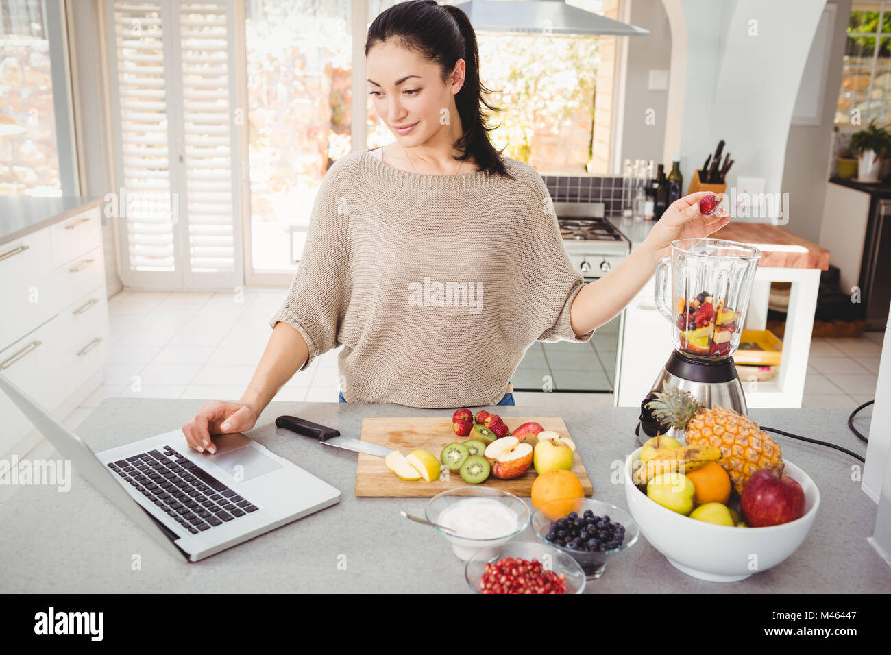 Woman preparing fruit juice while working on laptop Stock Photo - Alamy