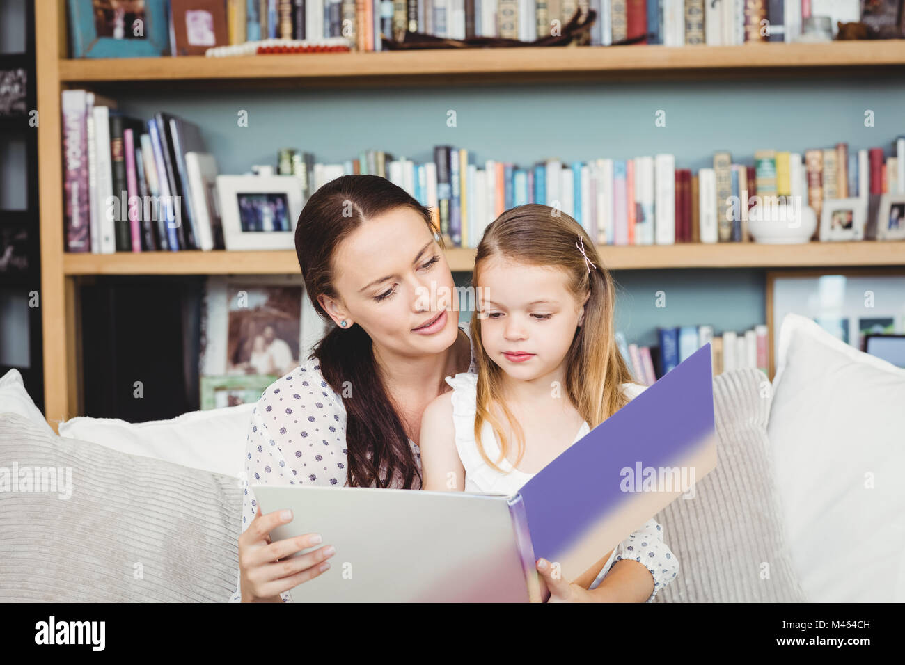 Mother and daughter reading book on sofa at home Stock Photo - Alamy