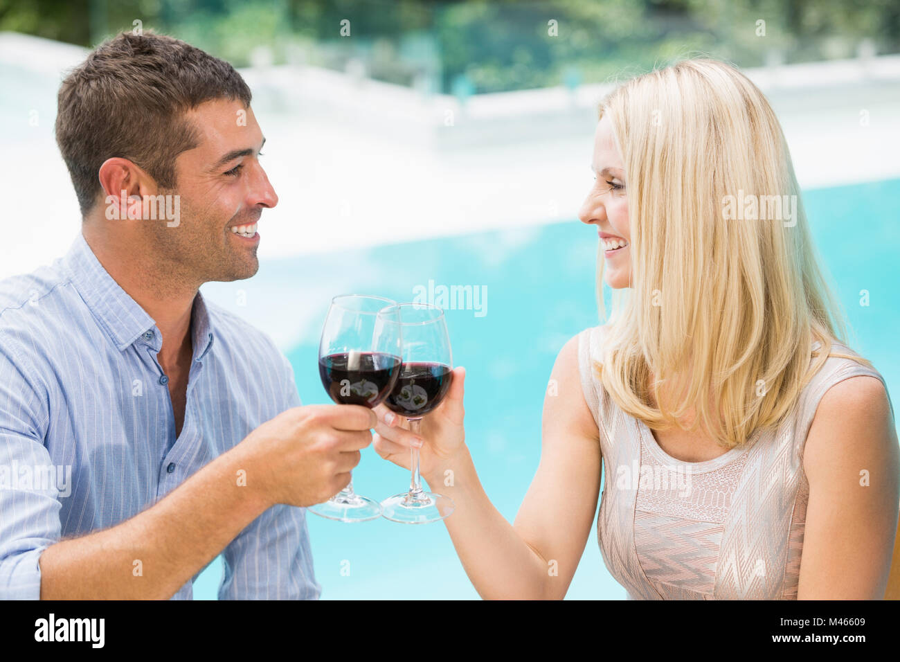 Smiling couple toasting red wine while sitting by swimming pool Stock ...