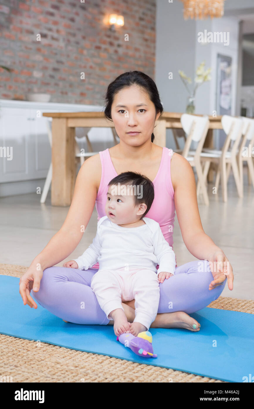 Serious woman sitting on mat with baby daughter Stock Photo - Alamy