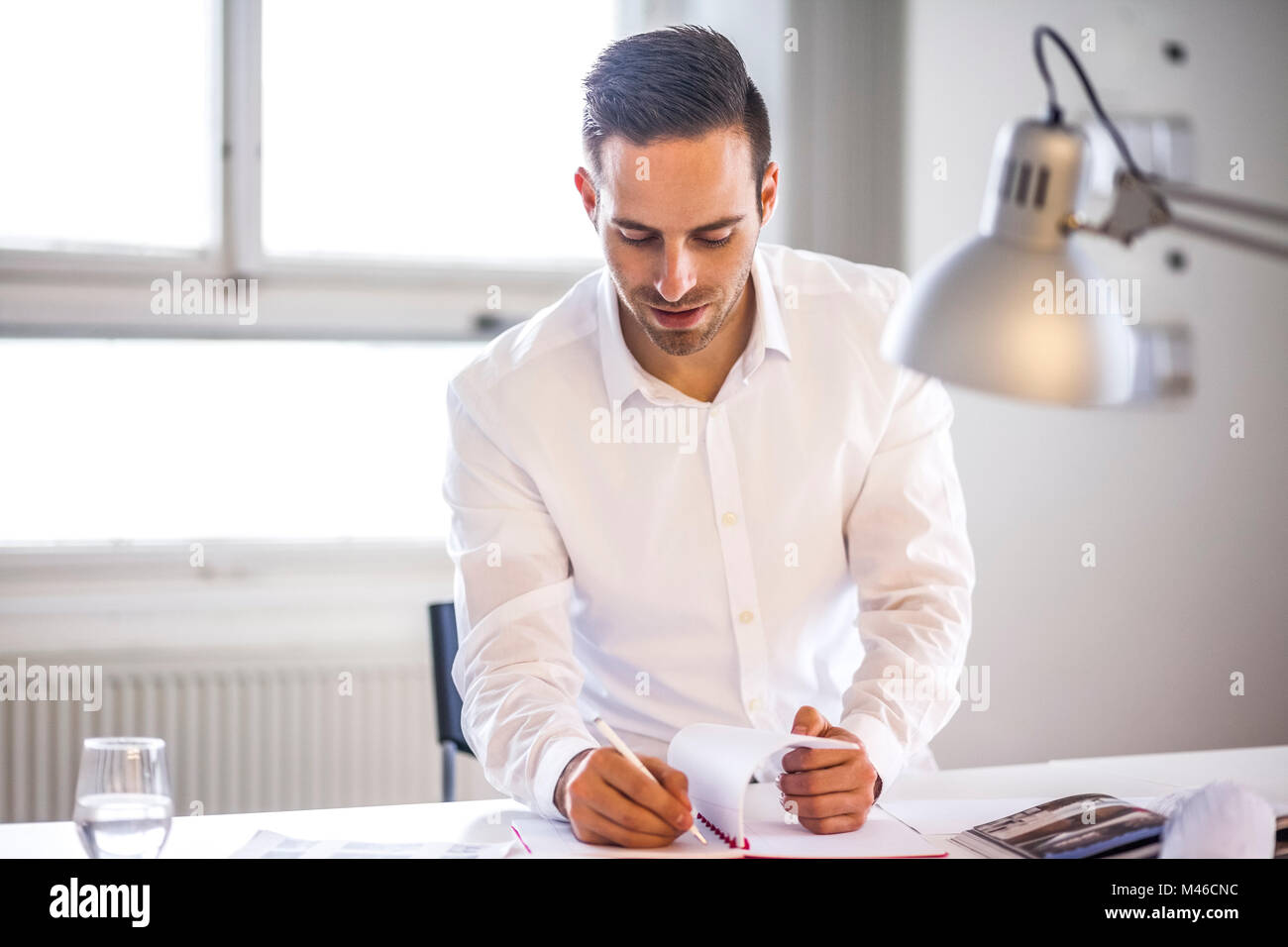 Young businessman writing notes at desk in office Stock Photo - Alamy