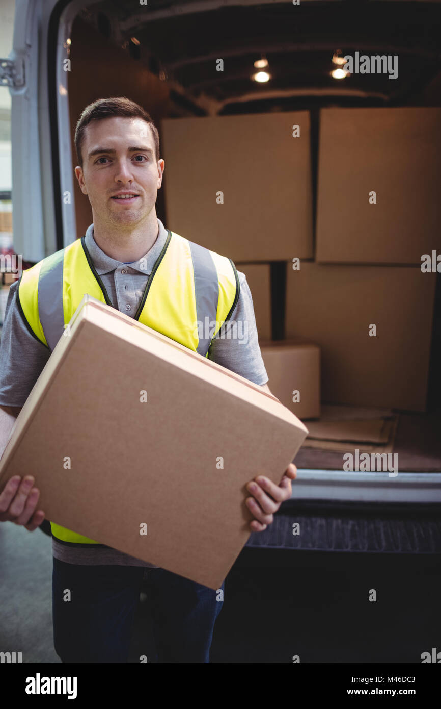 Delivery driver smiling at camera by his van holding parcel Stock Photo ...