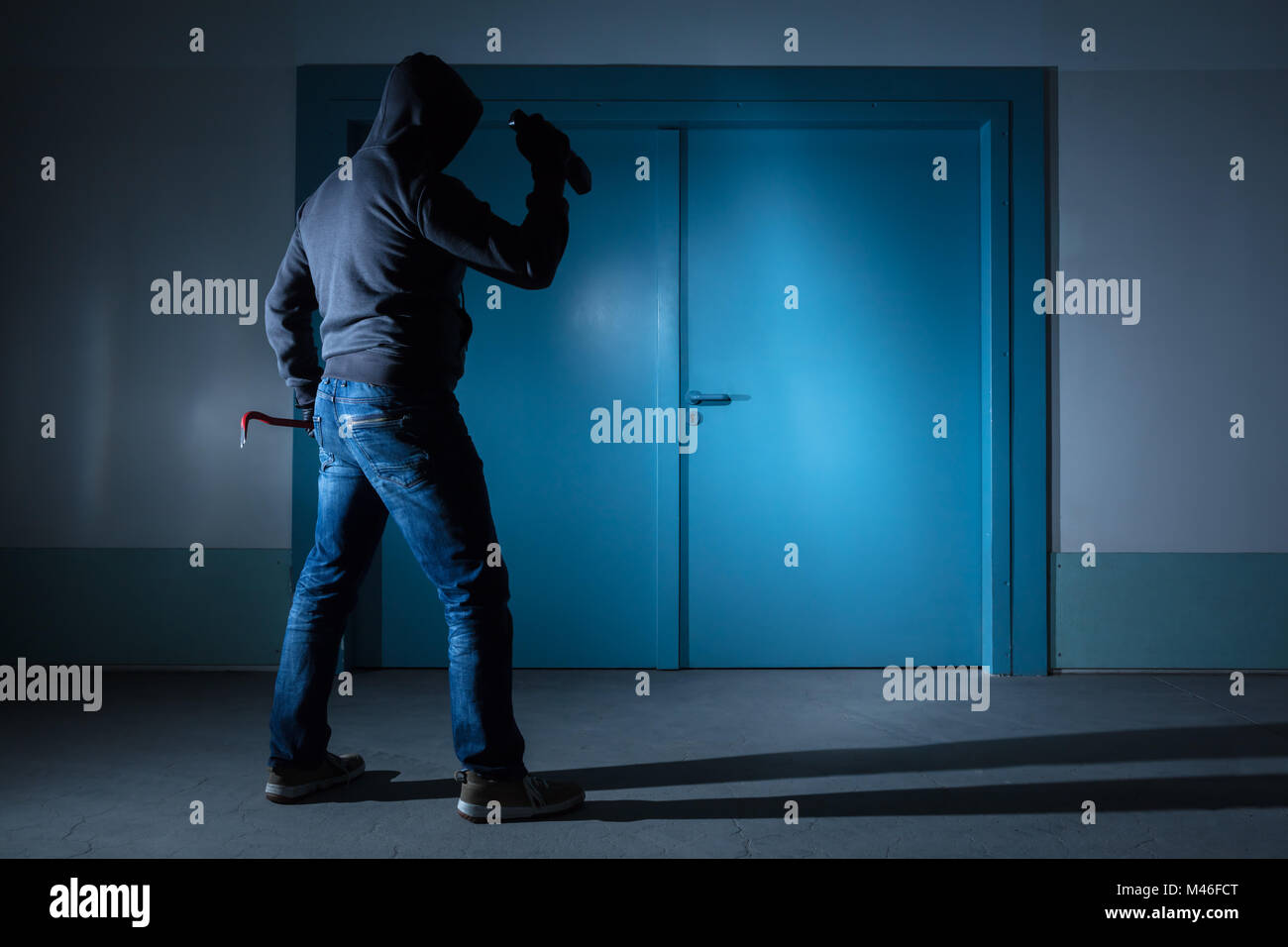 Rear View Of A Thief With Flashlight And Crowbar Standing Outside The ...