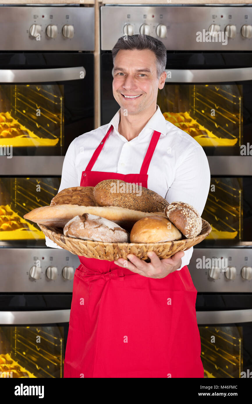 Smiling Baker Holding A Wicker Basket Full Of Bread In Front Of Oven ...