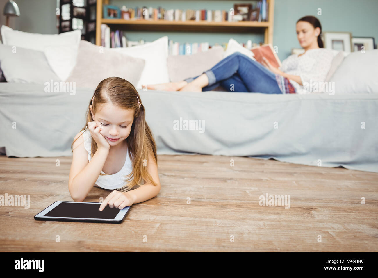 Girl using digital tablet with mother reading book Stock Photo - Alamy