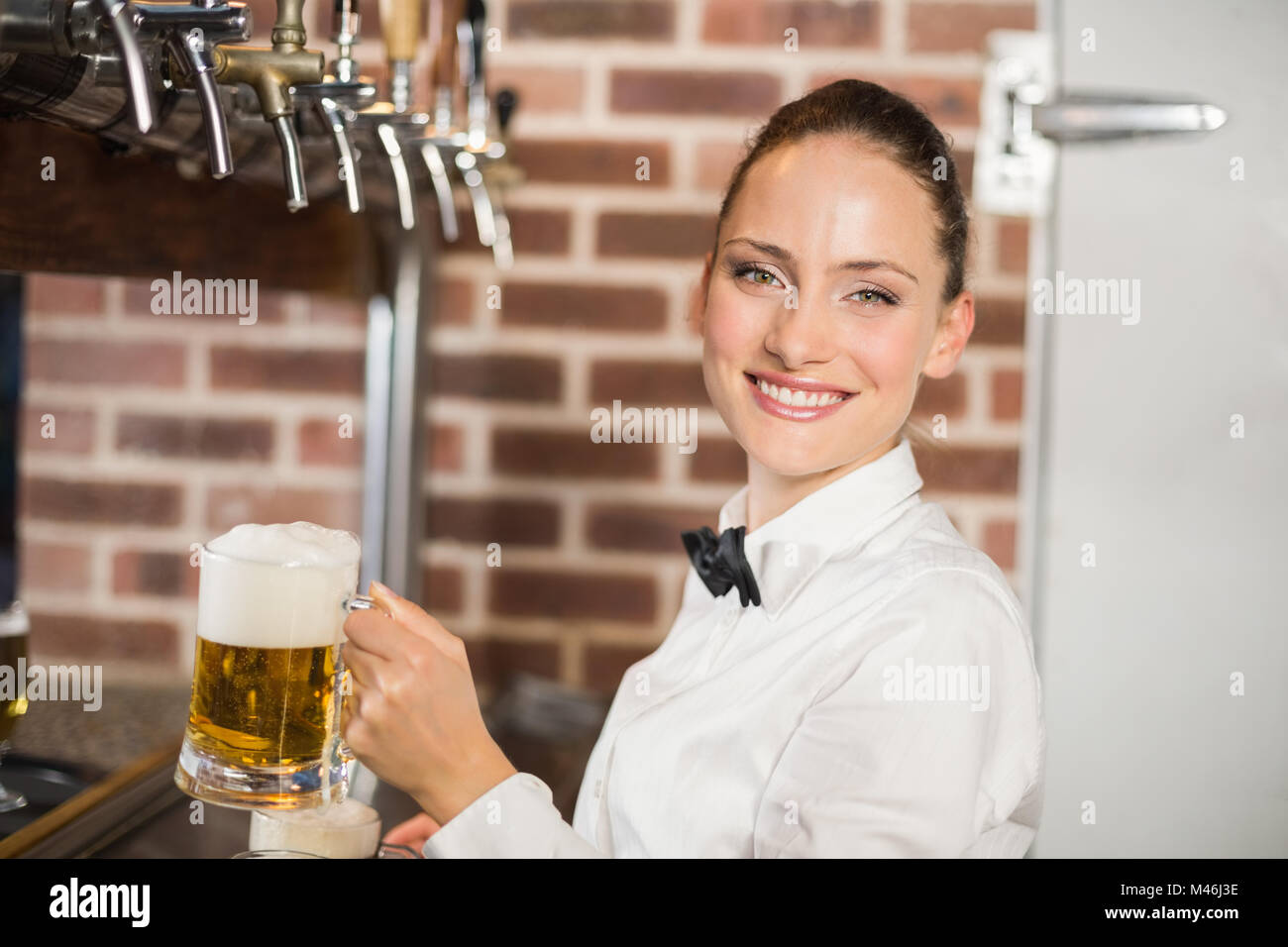 Barmaid holding beers while smiling at camera Stock Photo - Alamy