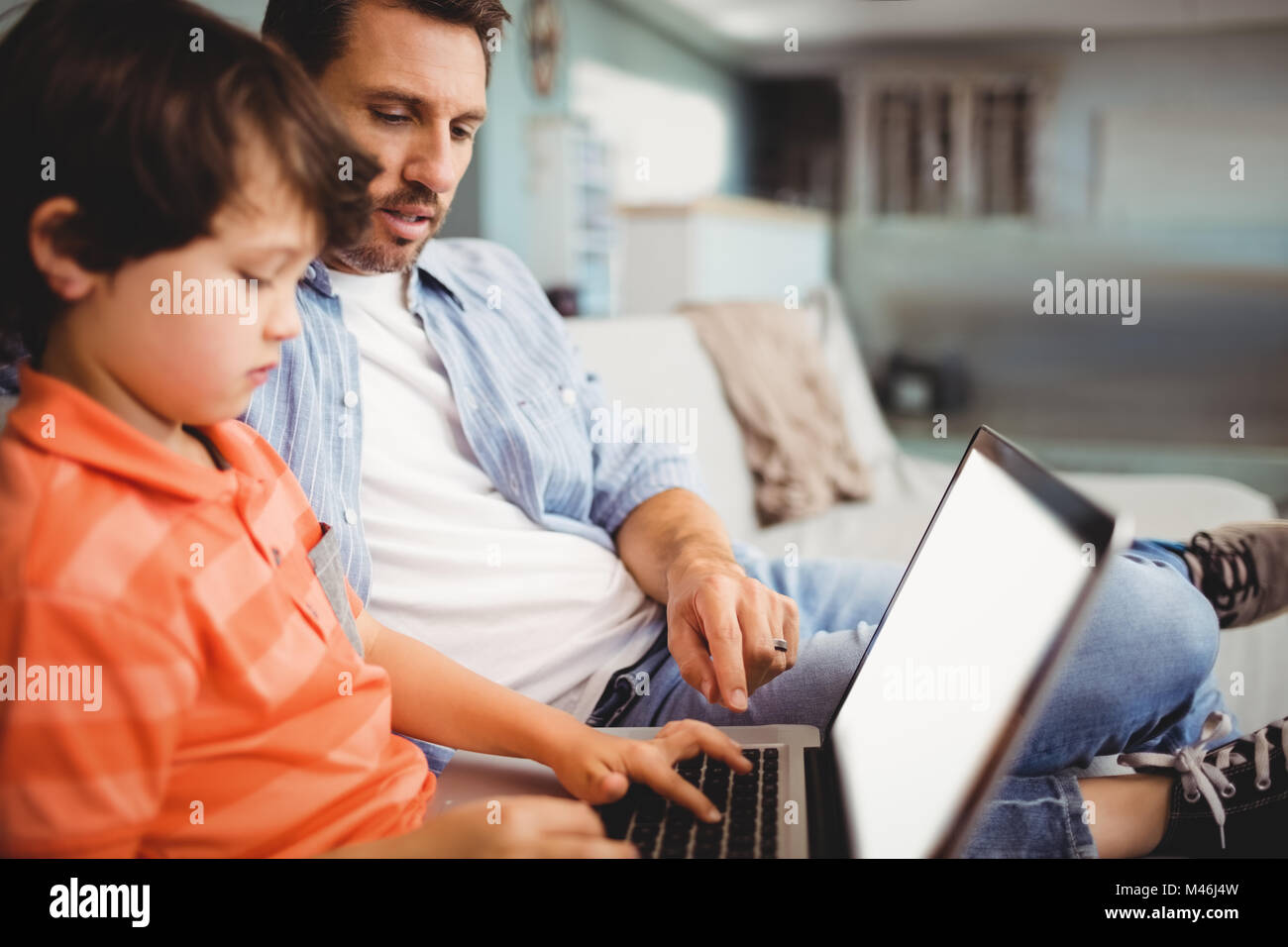 Father and son working on laptop while sitting on sofa Stock Photo - Alamy