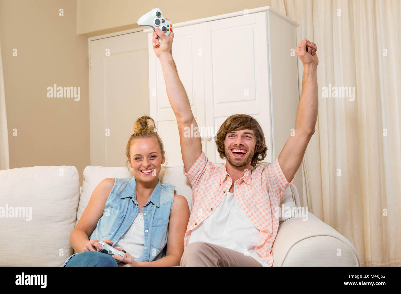 Cute couple playing video games sitting on the couch Stock Photo - Alamy