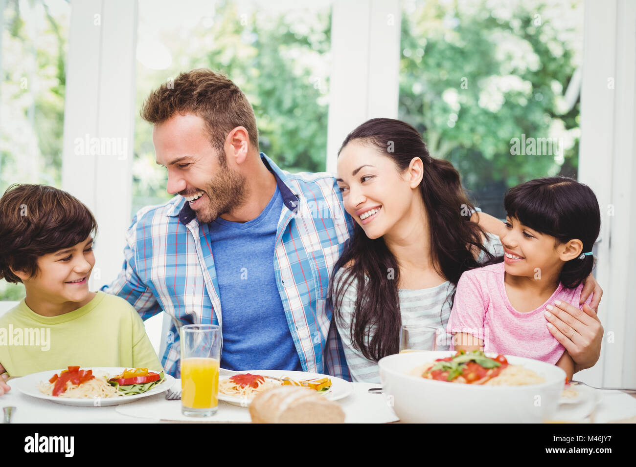 Smiling family with arm around while sitting at dining table Stock ...