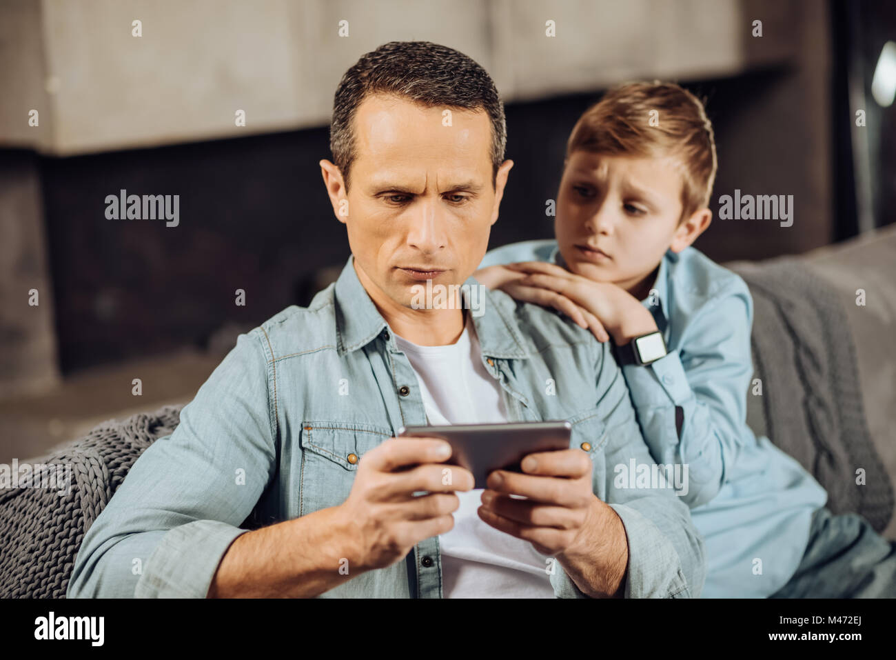 Sad boy watching his father play on phone Stock Photo - Alamy