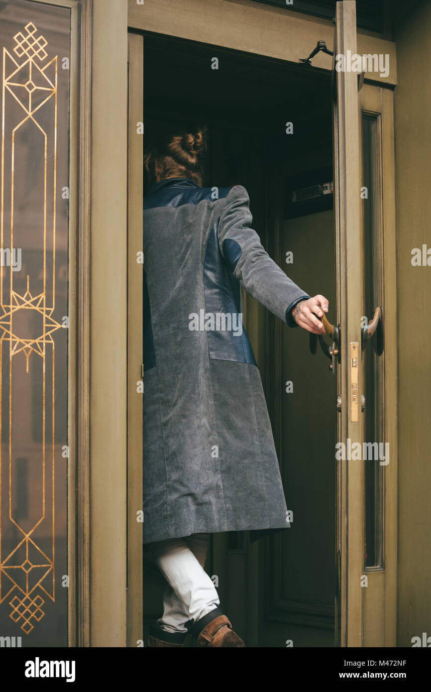 Portrait of a young bearded man dressed in coat enters a door in a cafe ...